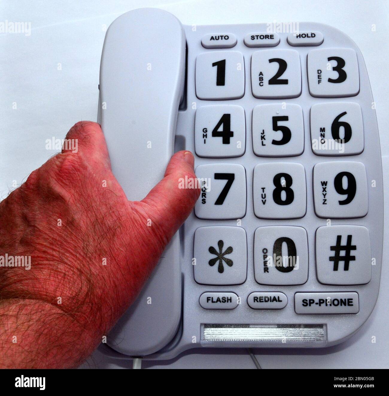 The hand of a senior or older man picks up the handset of a big button ...