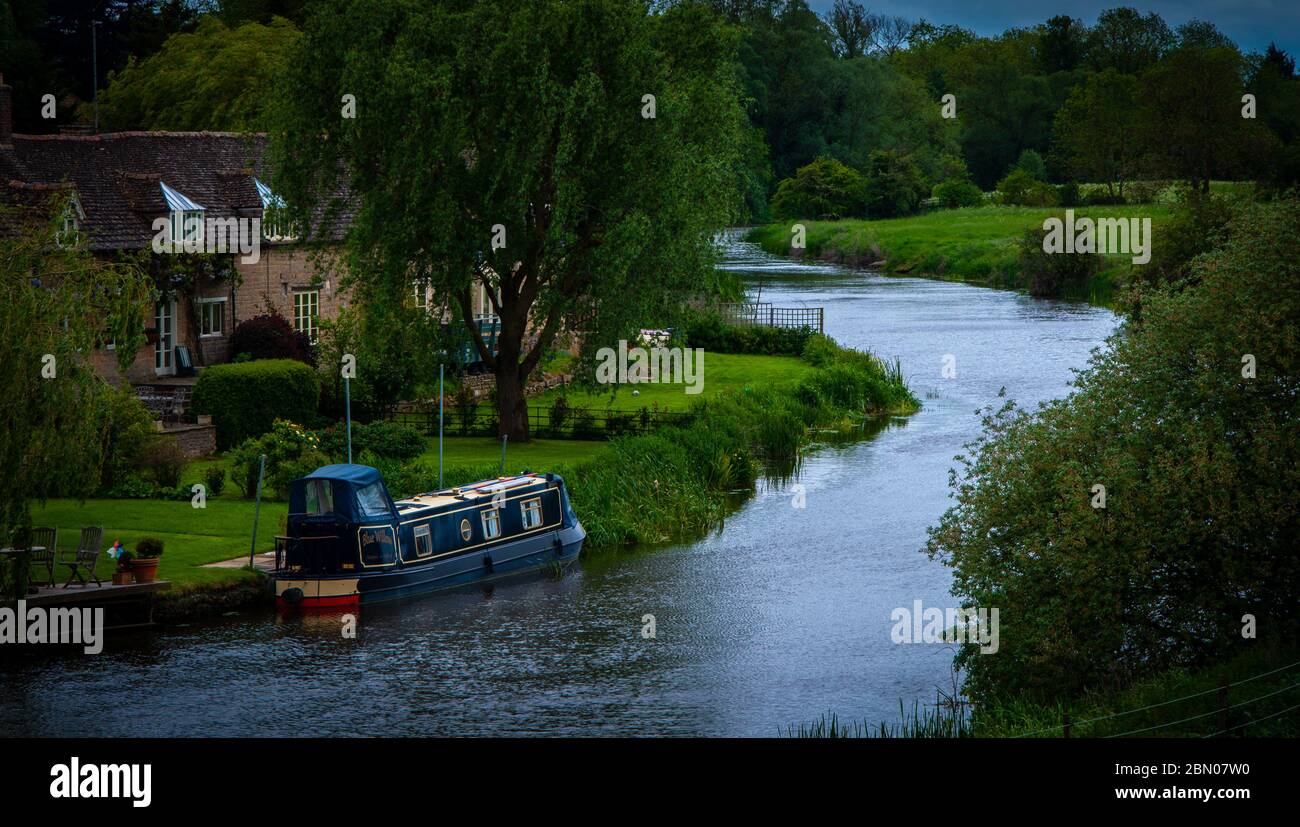 A blue narrowboat is moored alongside traditionally built stone houses ...