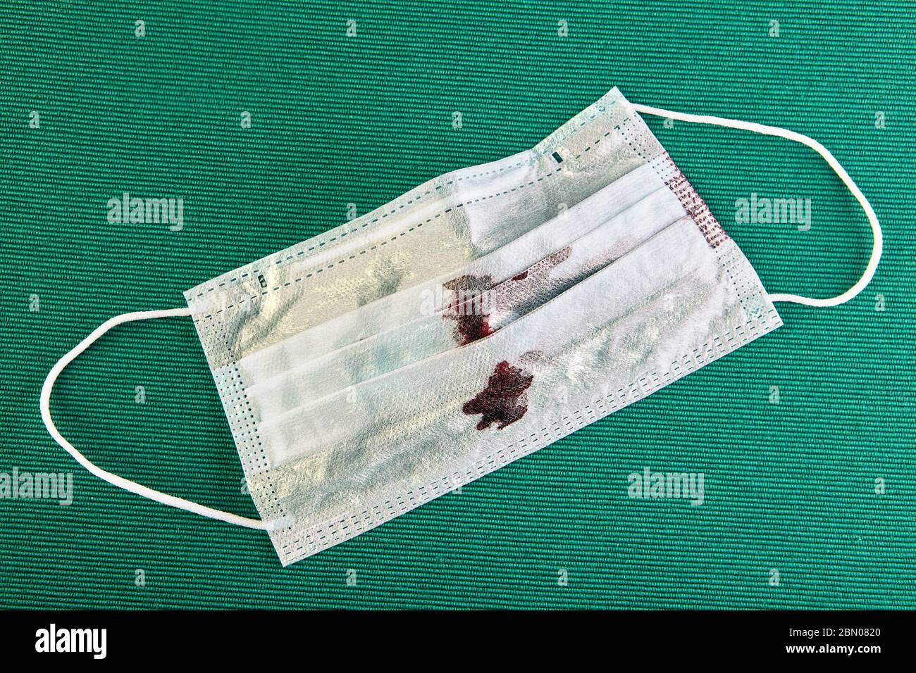 Blood stains on a disposable face mask, close-up, green background ...