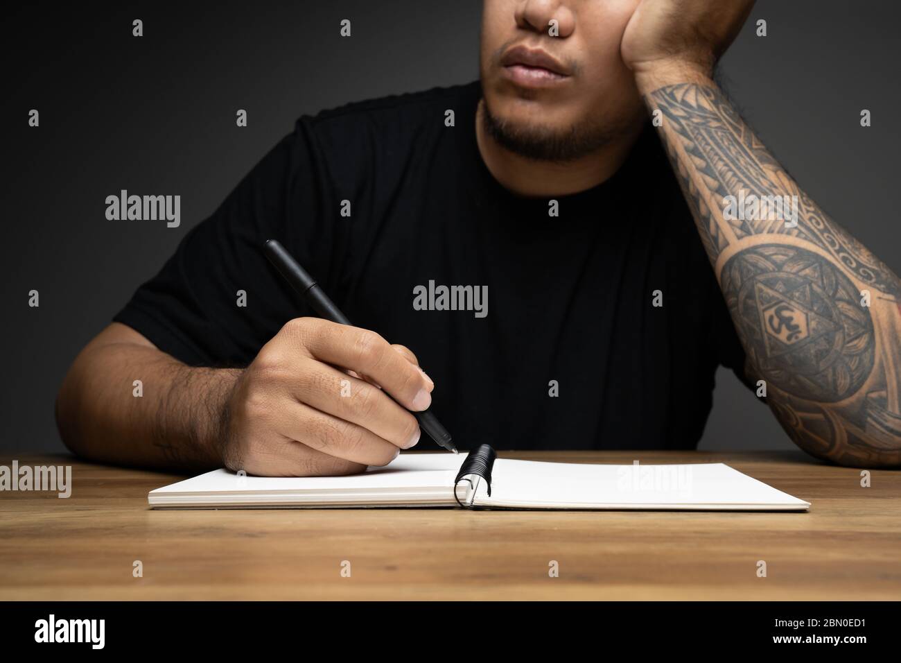 Asian man writing on a note book with boring face on wooden table ...
