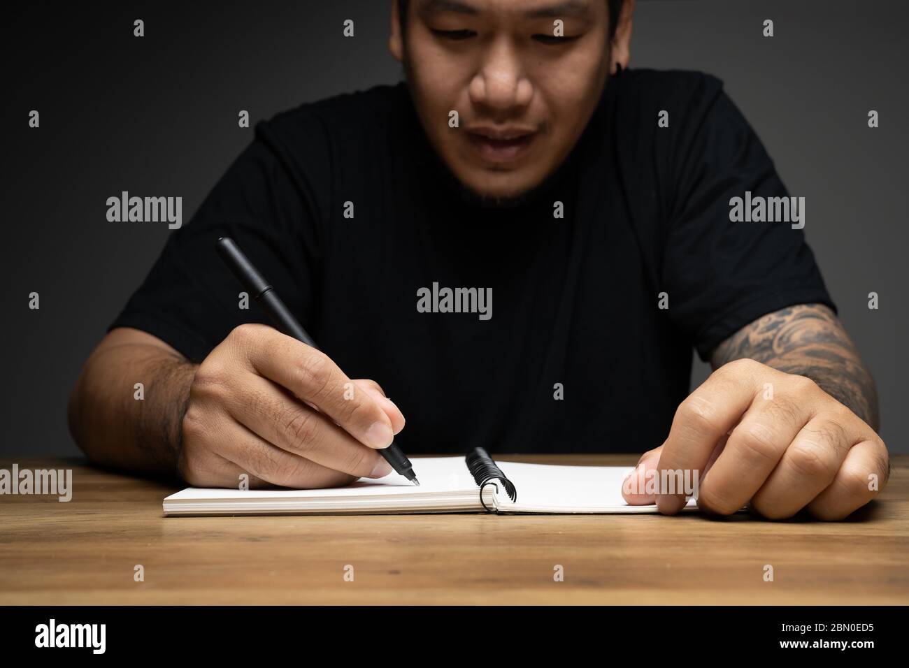 Asian man writing on a note book with focusing face on wooden table ...