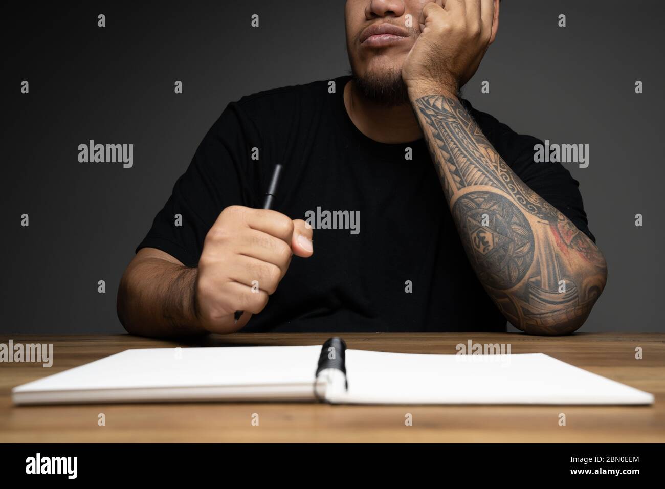 Asian man writing on a note book with thinking face on wooden table ...