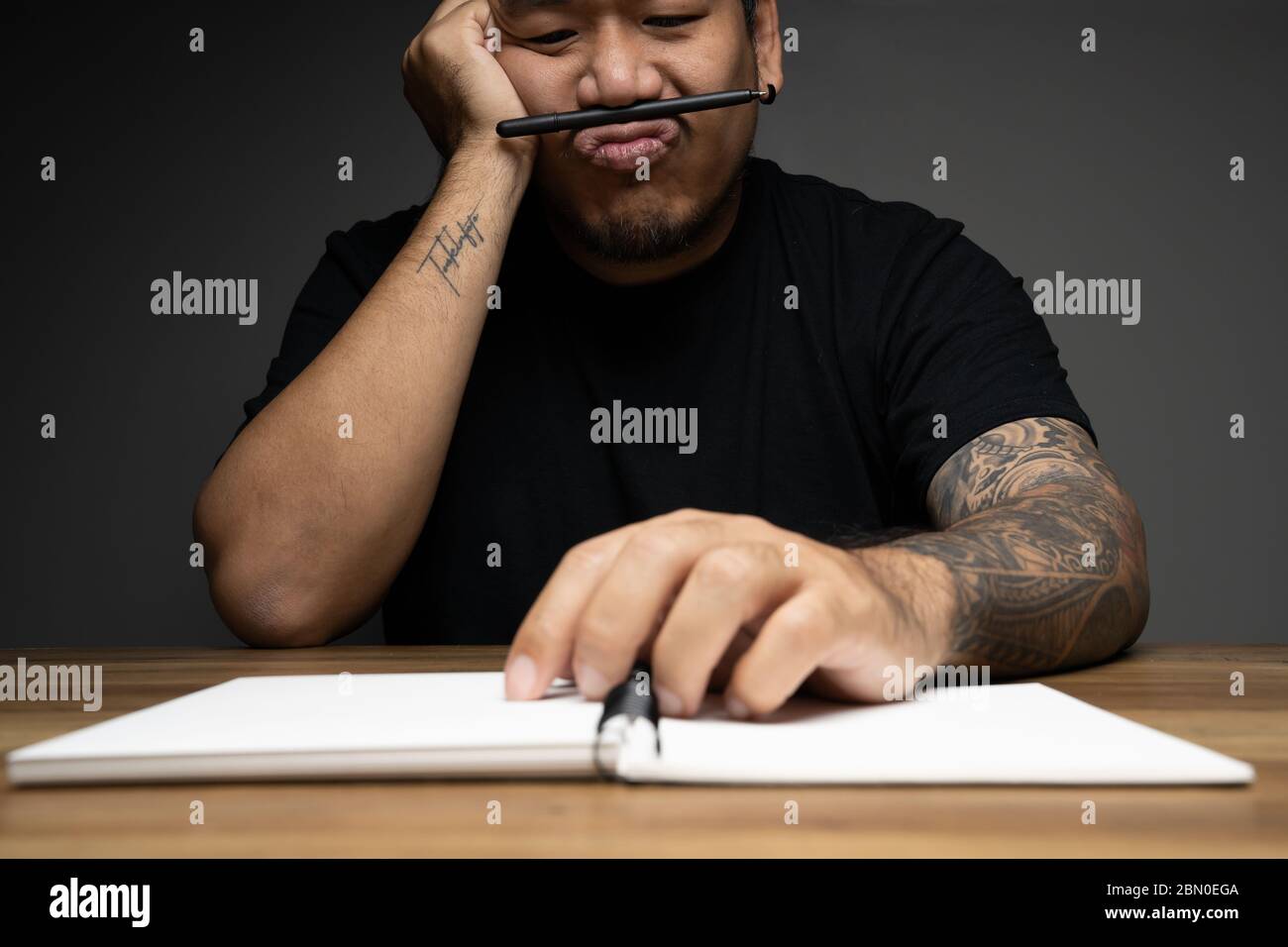 Asian man writing on a note book with thinking face on wooden table ...