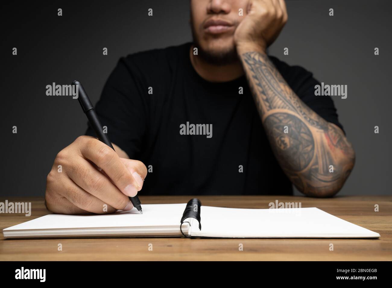 Asian man writing on a note book with boring face on wooden table ...