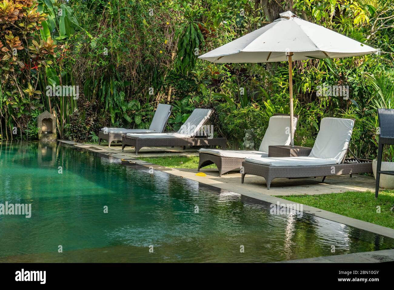 Balinese resort pool with chairs and umbrella Stock Photo - Alamy