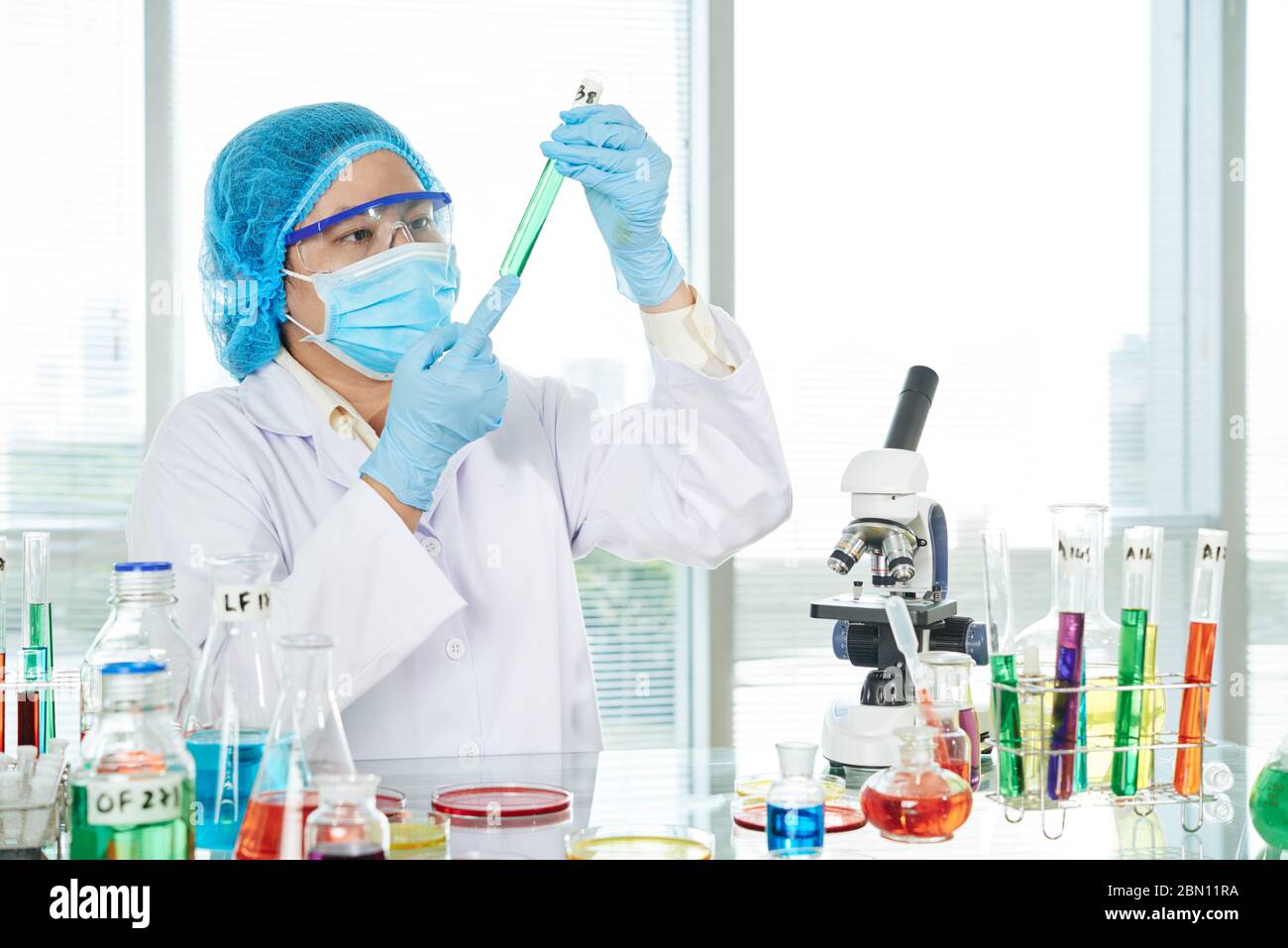 Laboratory technician in protective glasses looking at test-tube with ...