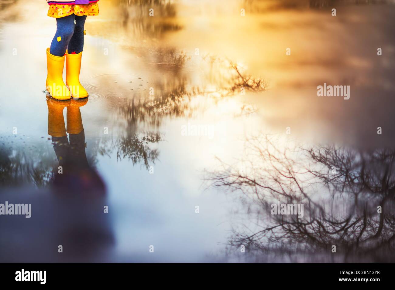 Happy child girl with yellow rubber boots jumping in puddle at the ...
