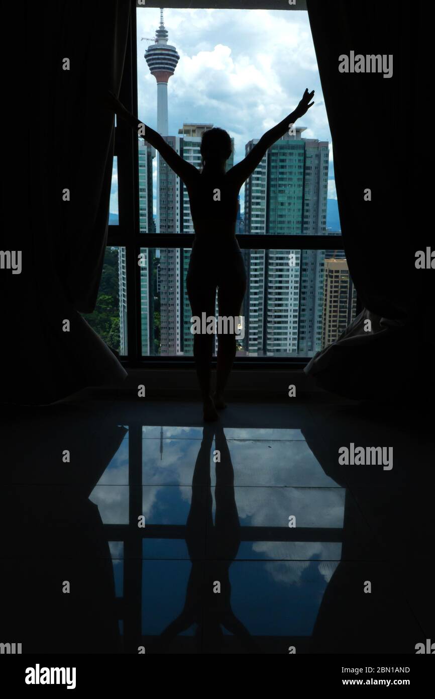 A slender girl is looking at the city through a large window. High ...