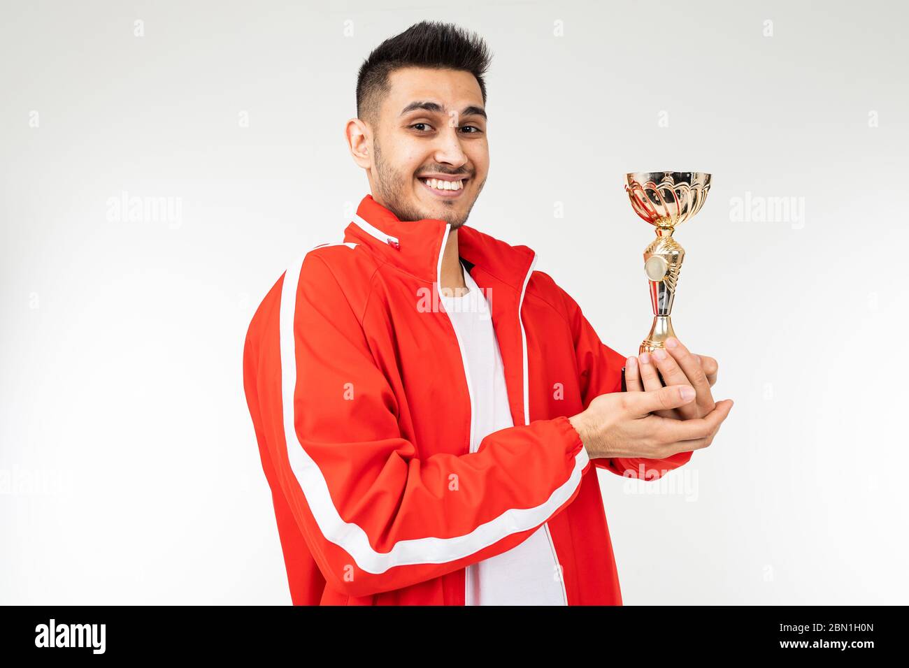 happy athlete in tracksuit with a golden winner cup on a white studio ...