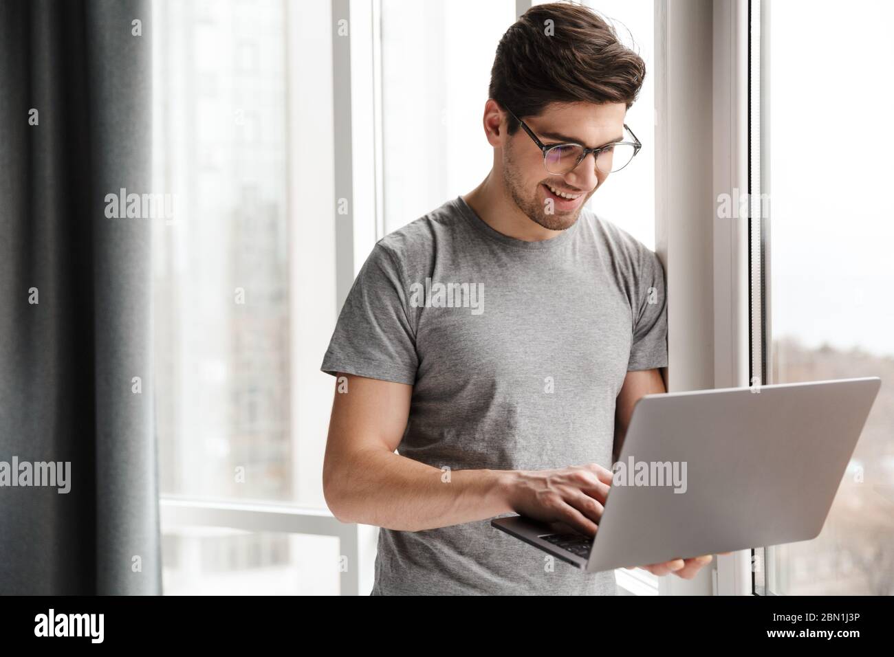 Image of a positive optimistic young man indoors at home using laptop ...