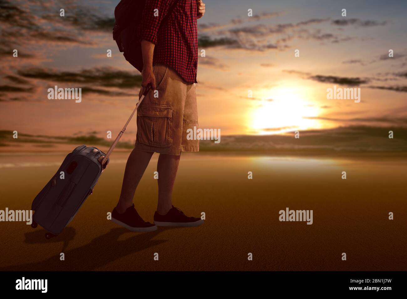 Man with backpack and suitcase traveling to the beach with a sunset sky ...