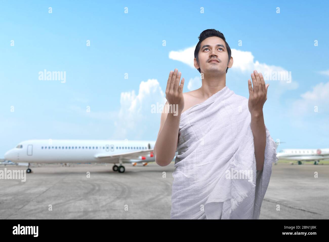 Asian Muslim man in ihram clothes standing and raised arms going to ...