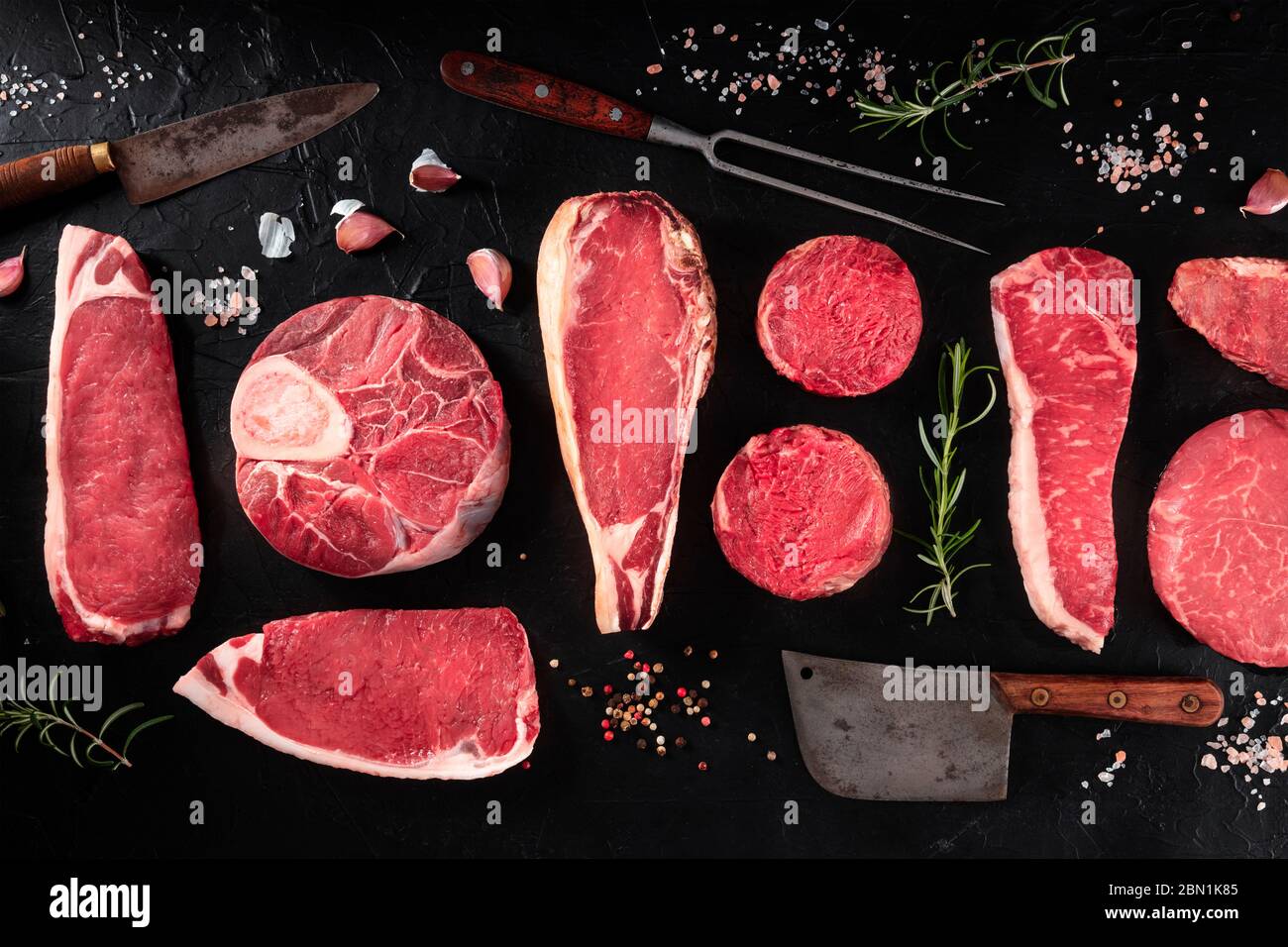 Cuts of meat, overhead flat lay shot on a dark background with salt ...