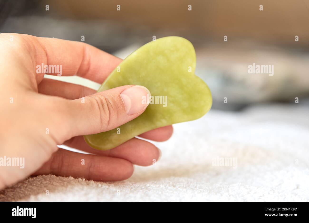 Female hand holding green gua sha facial massager Stock Photo - Alamy