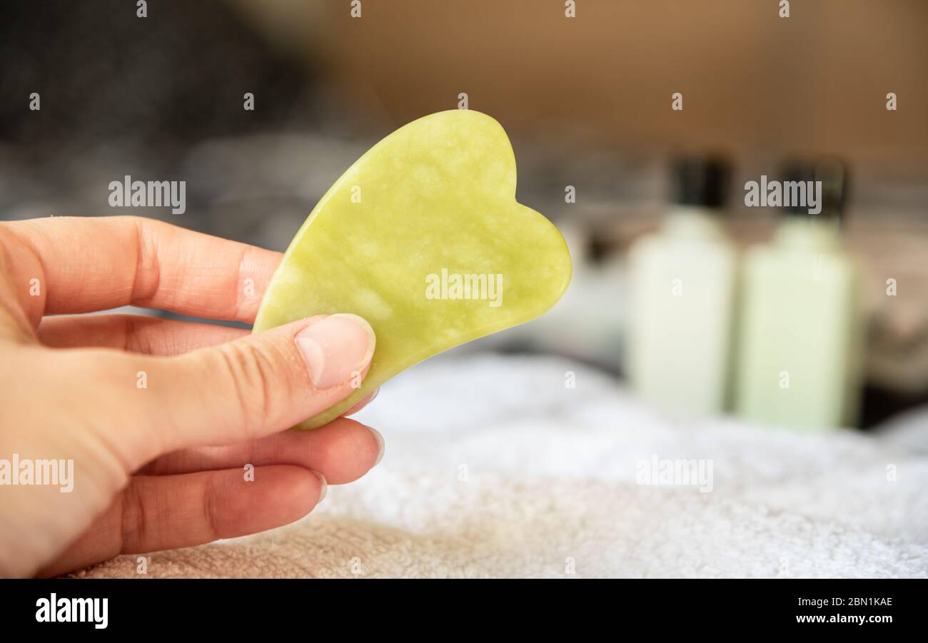Female hand holding green jade gua sha tool for self massage at home ...