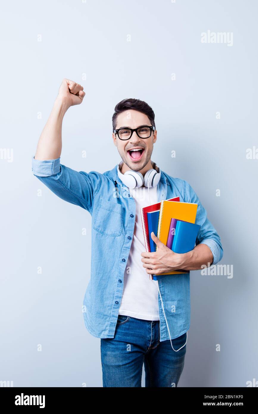 Cheerful young nerdy student is standing with books on pure background ...