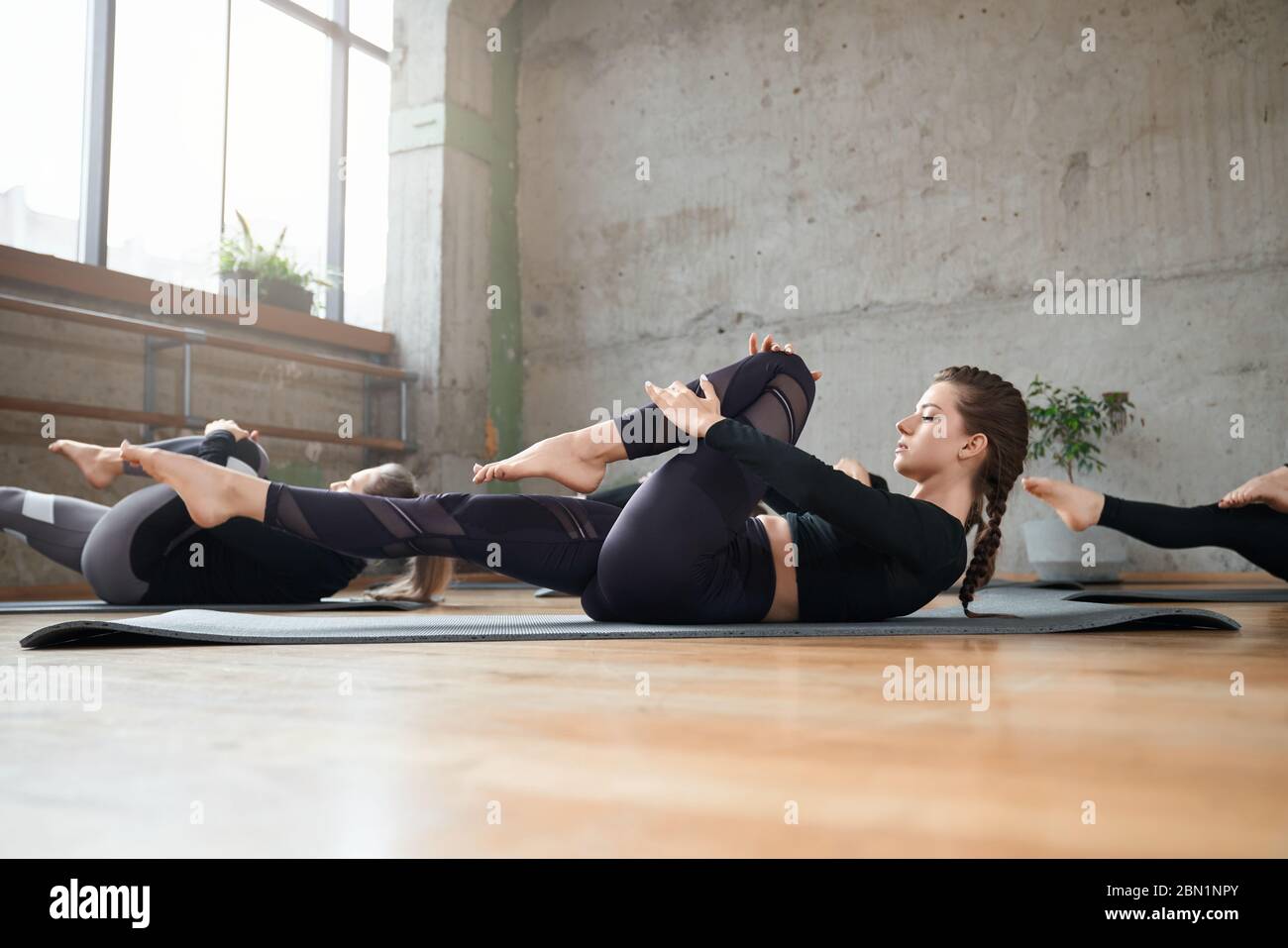 Side view of young fitnesswomen in sportswear lying in Knee to Chest ...