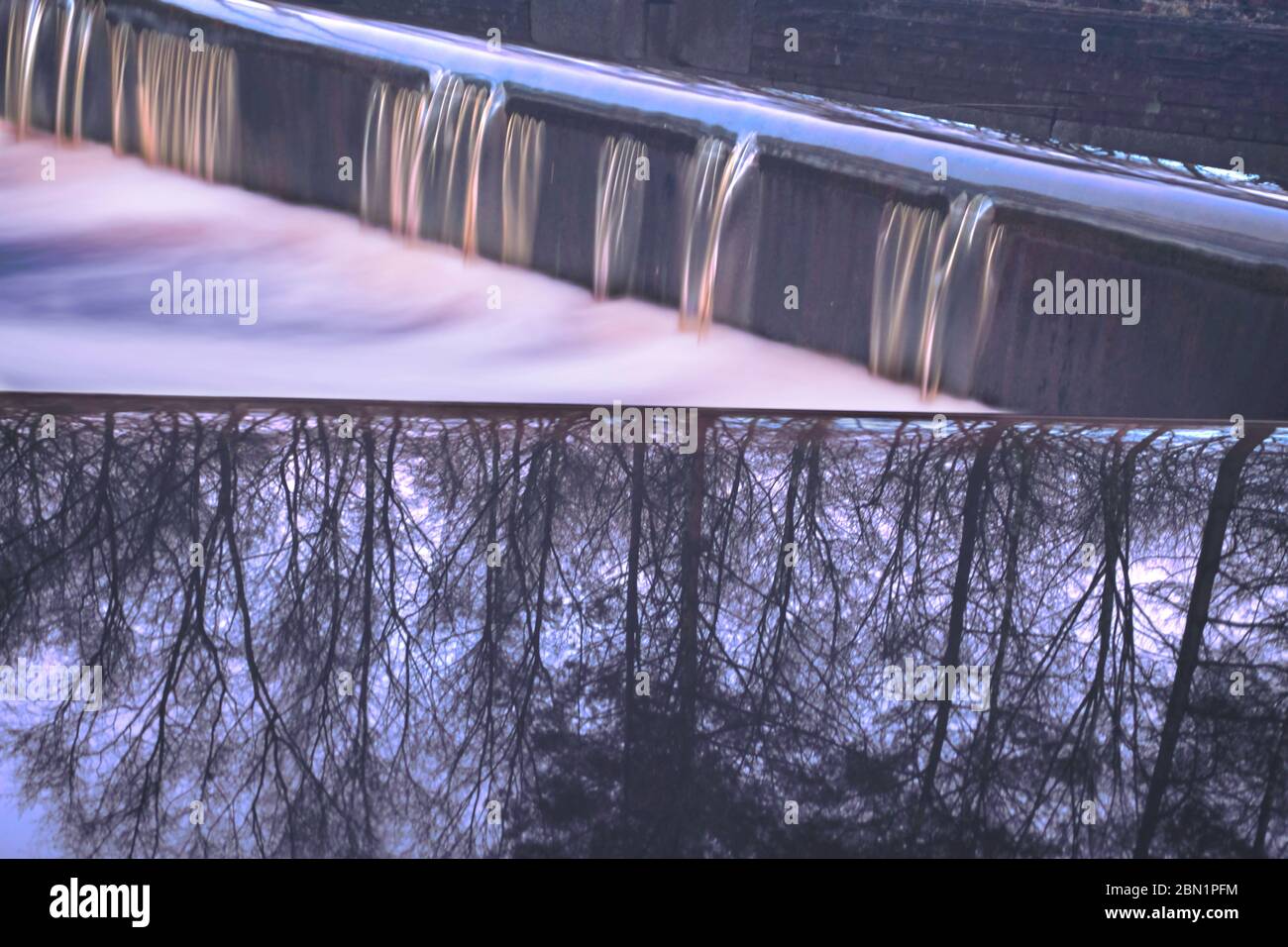 In a weir a lot of water flows along the weir, reflection of trees in ...