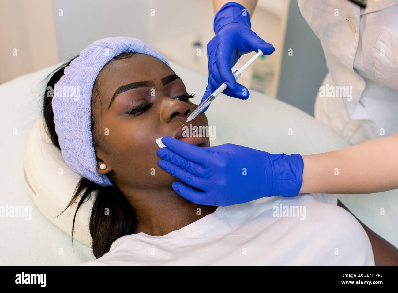 Pretty young African Woman receiving a botox injection in the lips zone ...