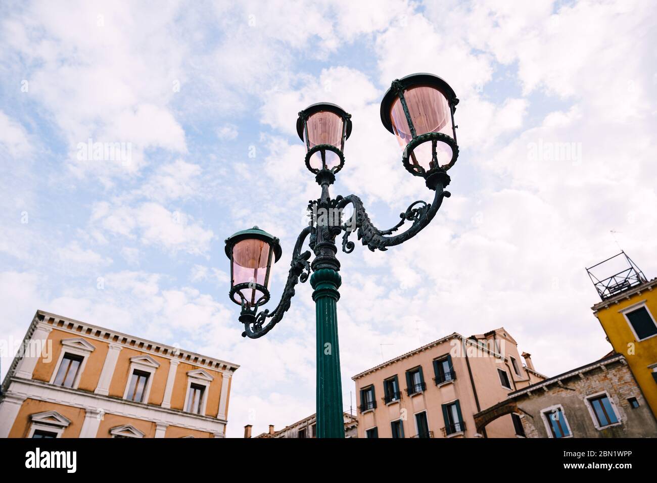 An ancient triple metal street lamp, with pink plafonds against the sky ...