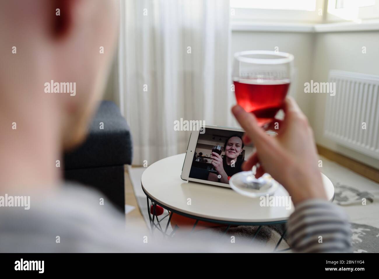 Man drinking red wine online with female friend using tablet pc at home ...