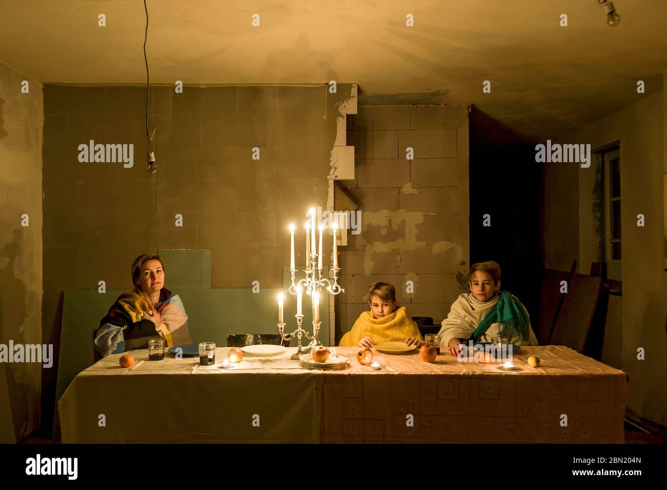 four membered family sitting down at the long table by candlelight ...