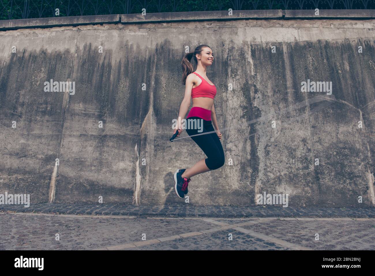 Cheerful young lady in stylish training outfit is jumping with jump ...