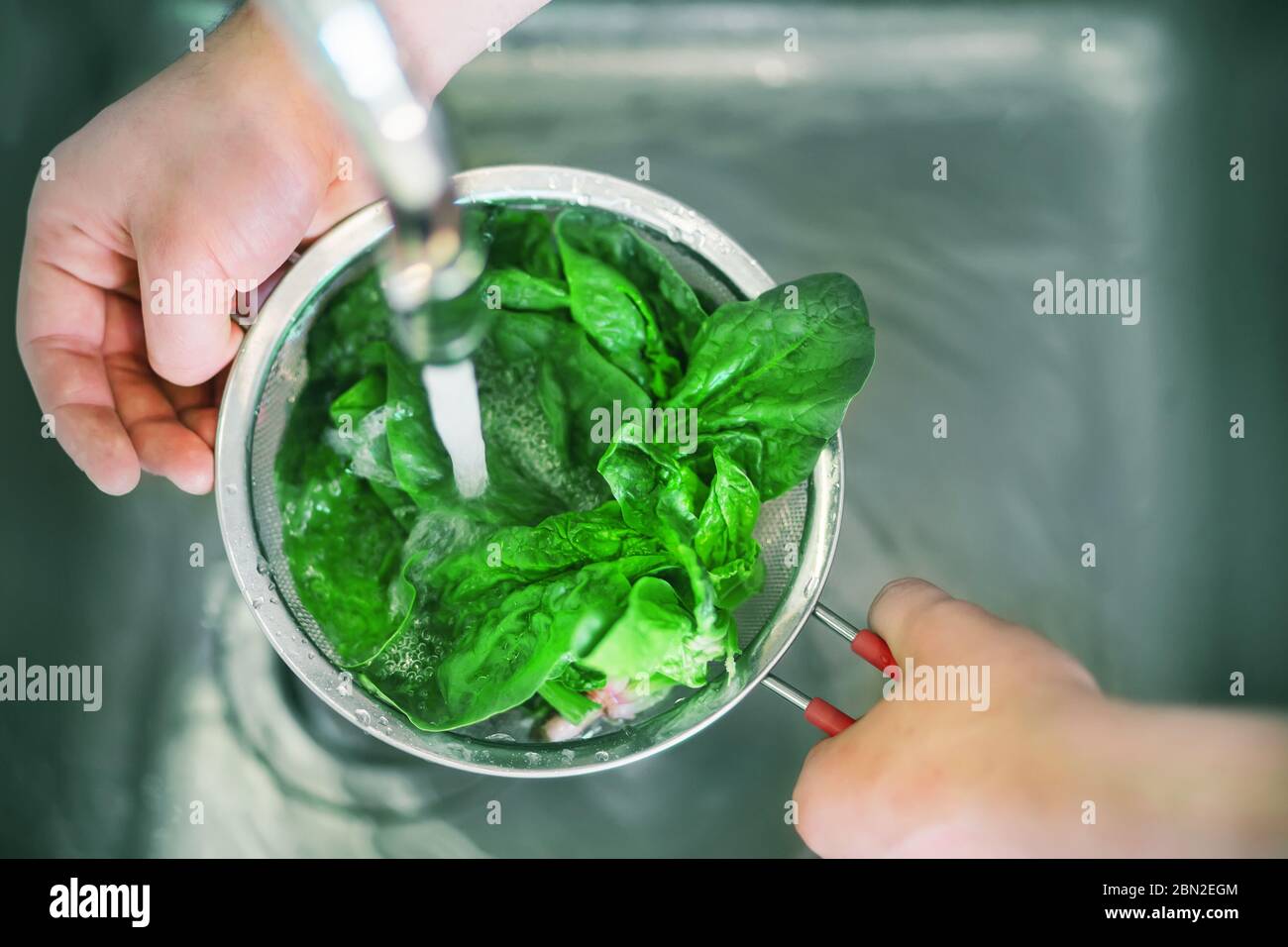 A man holds a colander with a red handle under the flow of water from ...
