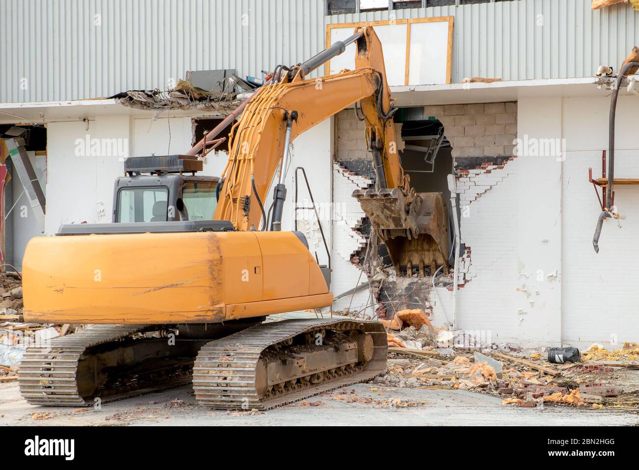 A backhoe demolishing a building, The bucket is in a hole in the wall ...