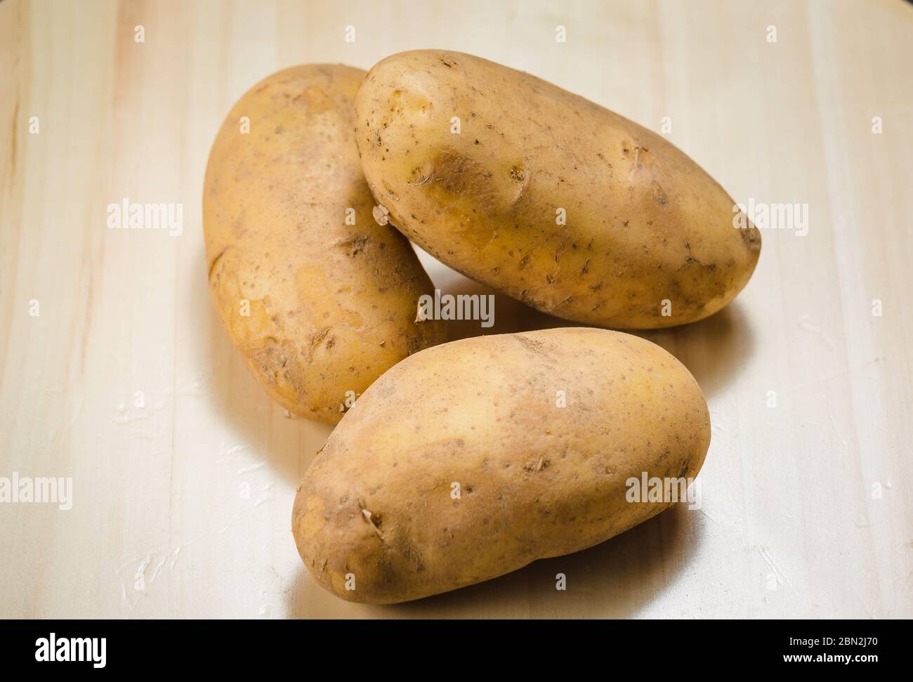 three potatoes on a light wooden Stock Photo - Alamy