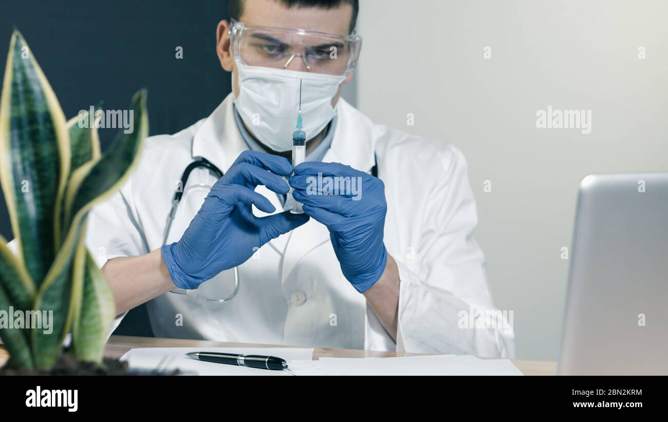 Doctor preparing vaccine syringe for injection and looking at needle ...