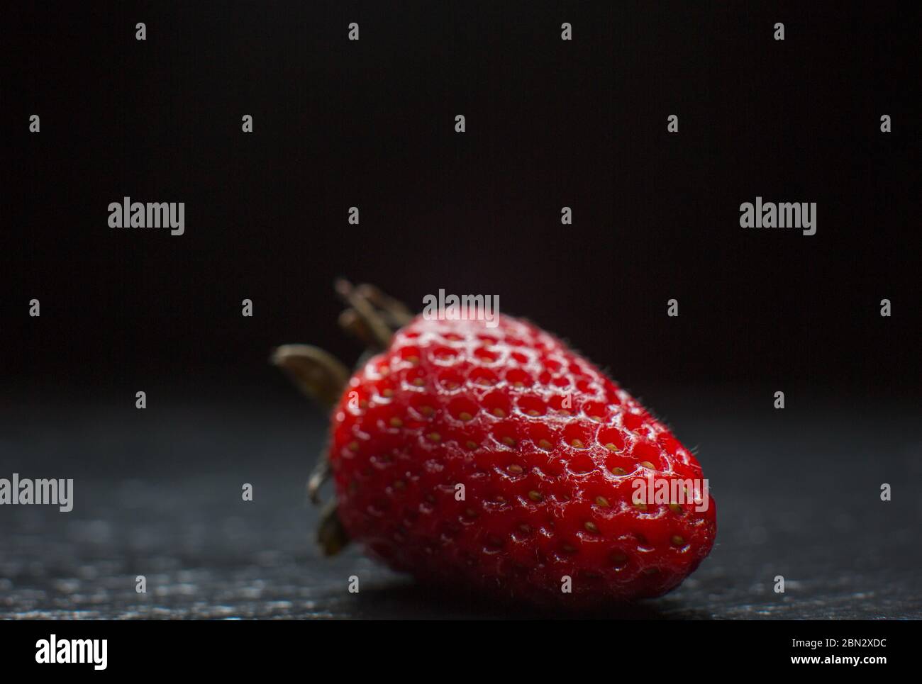 A close up macro photograph of a whole fresh ripe organic strawberry on ...