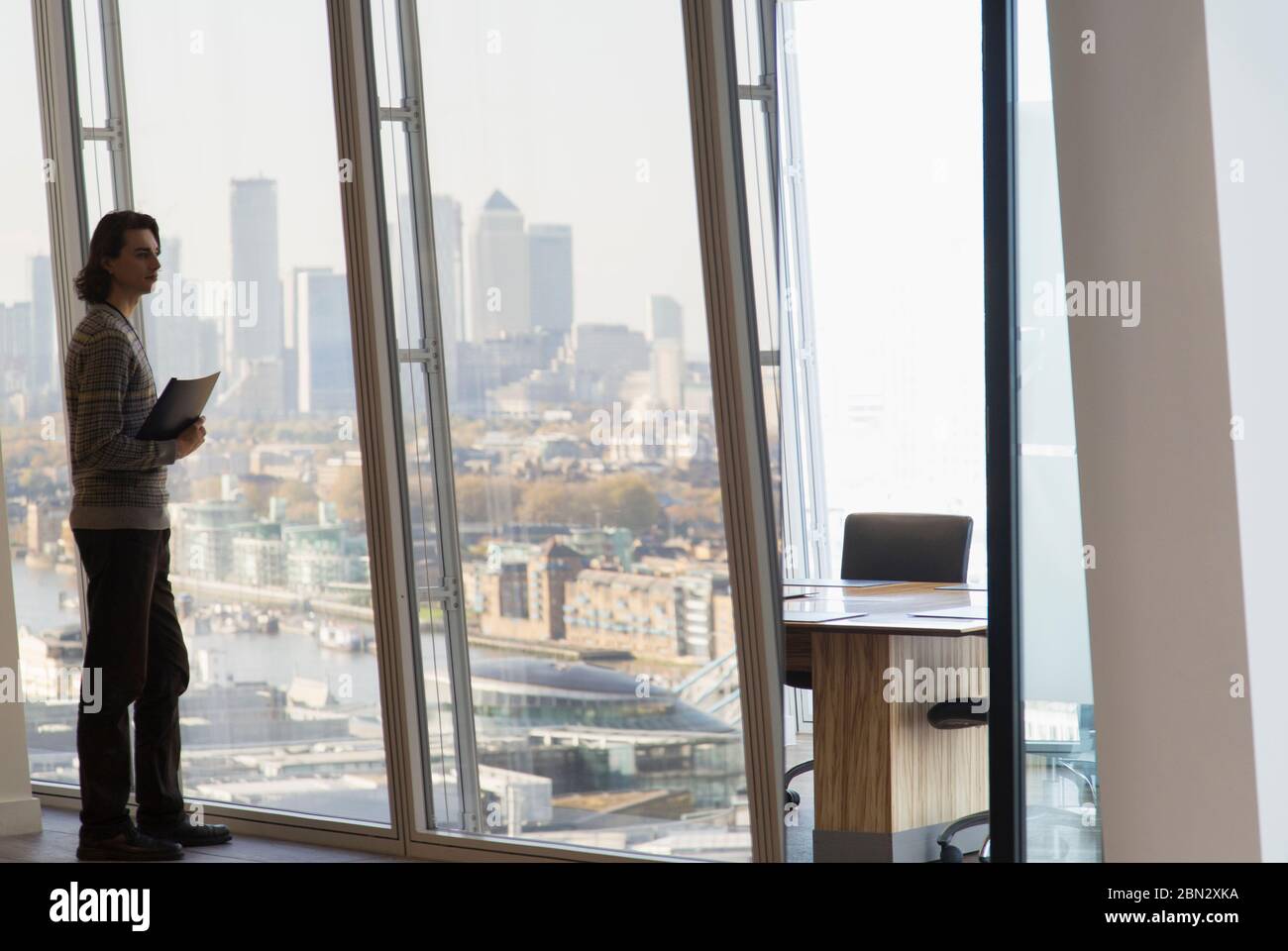 Thoughtful businessman standing at urban highrise office window Stock ...