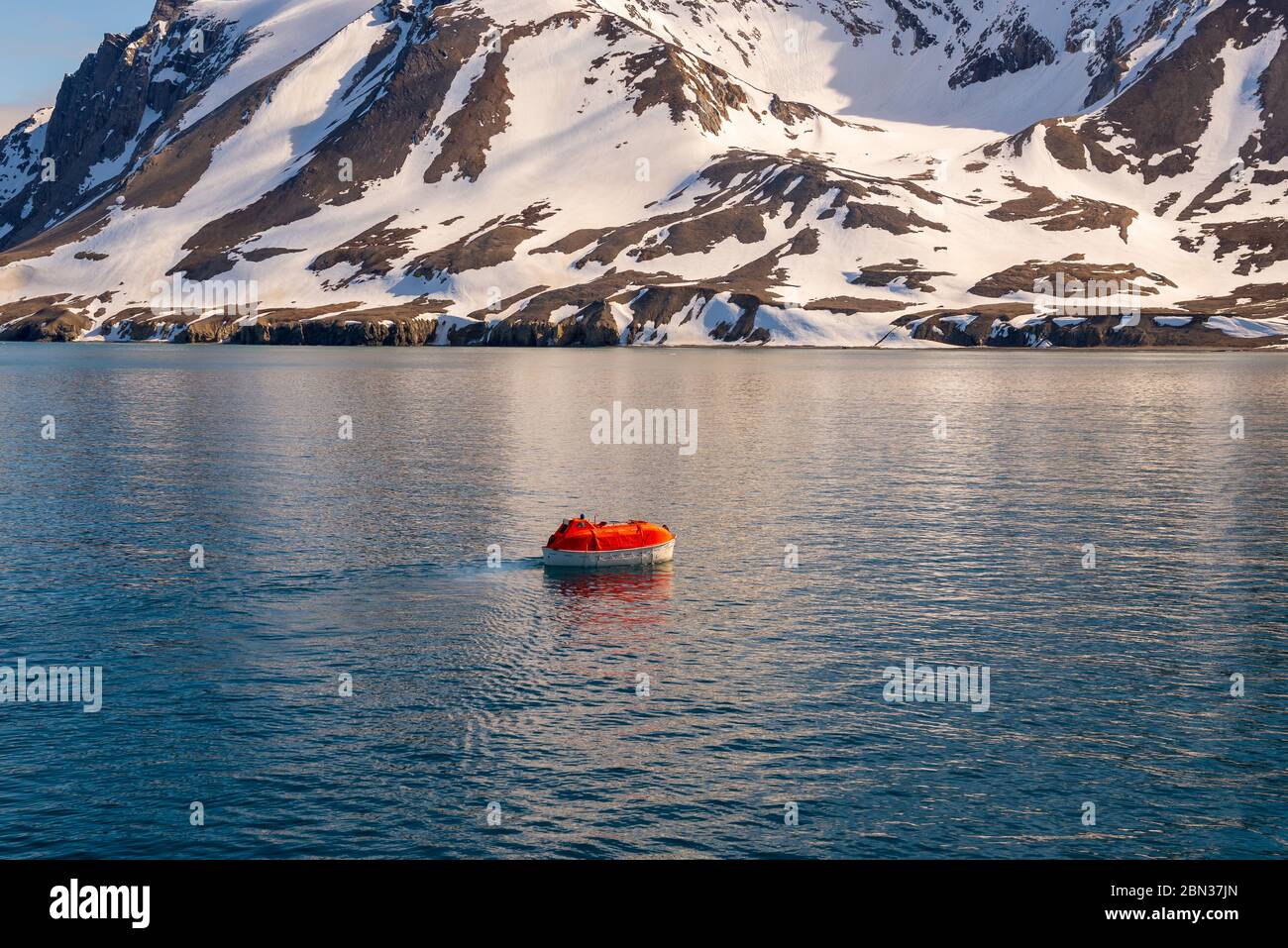 Lowering orange lifeboat to water in Arctic waters, Svalbard. Abandon ...