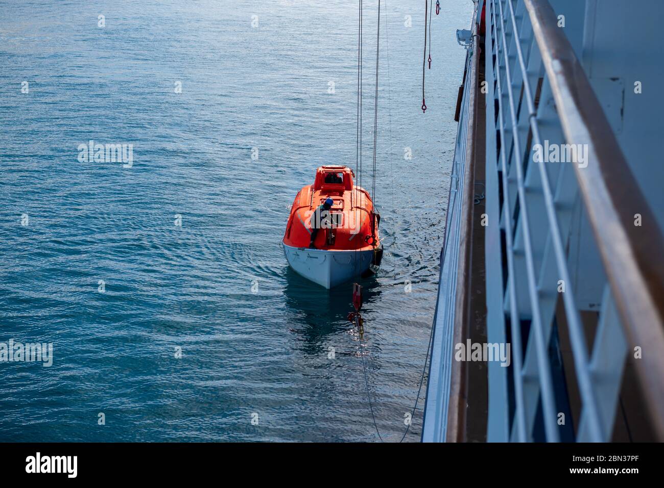 Lowering orange lifeboat to water in Arctic waters, Svalbard. Abandon ...