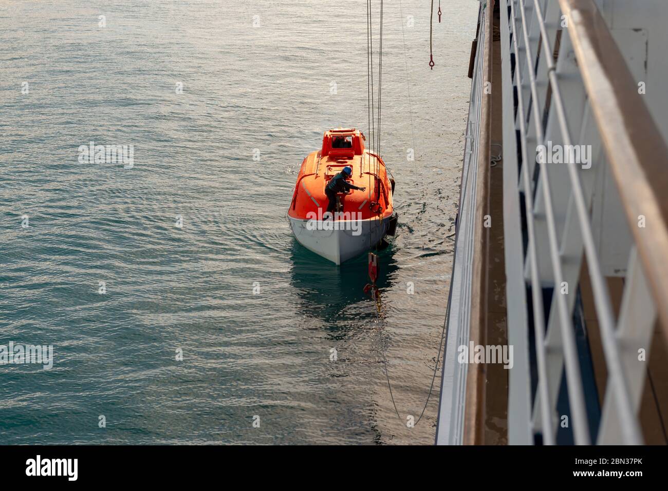 Lowering orange lifeboat to water in Arctic waters, Svalbard. Abandon ...