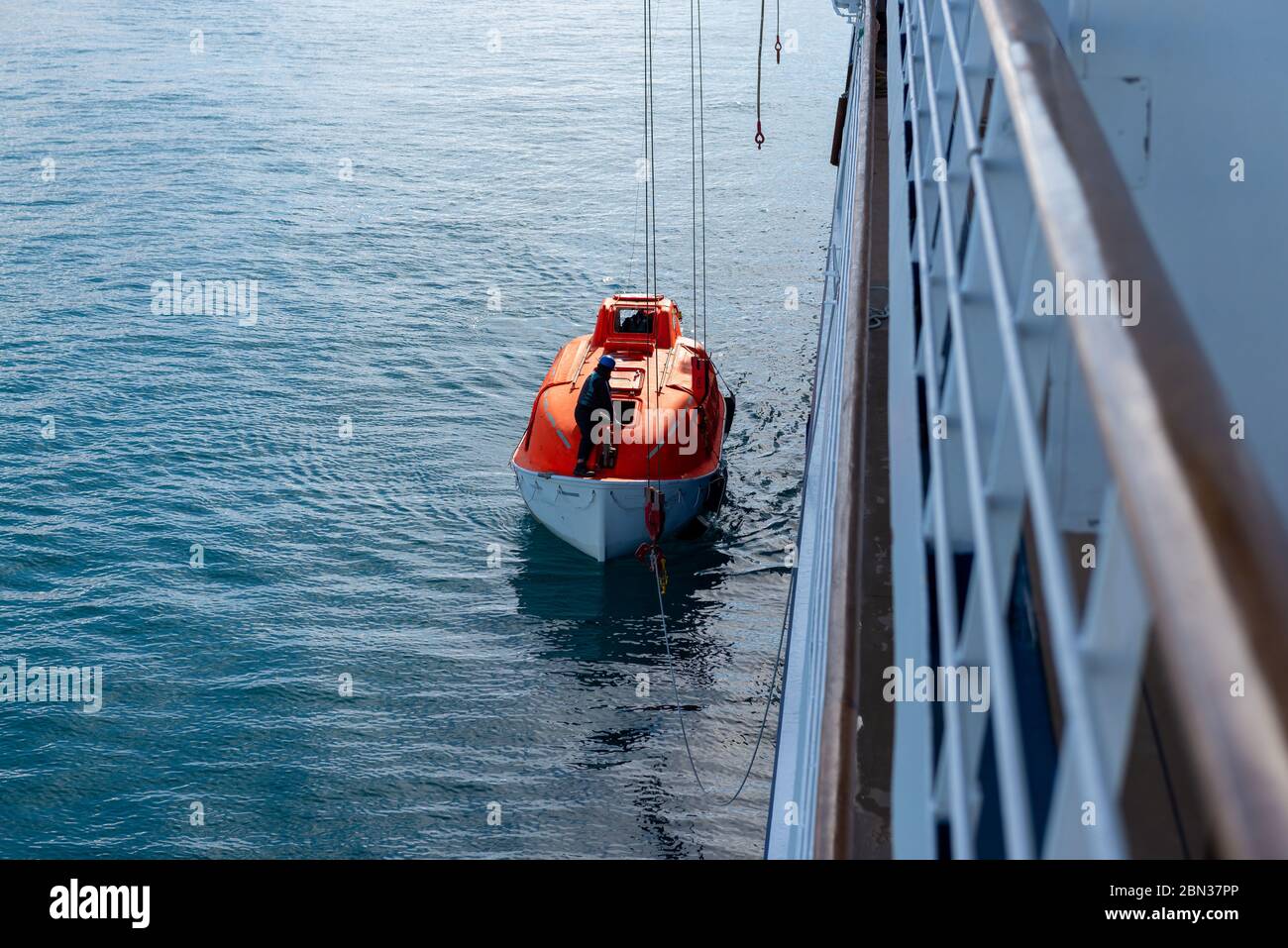 Lowering orange lifeboat to water in Arctic waters, Svalbard. Abandon ...