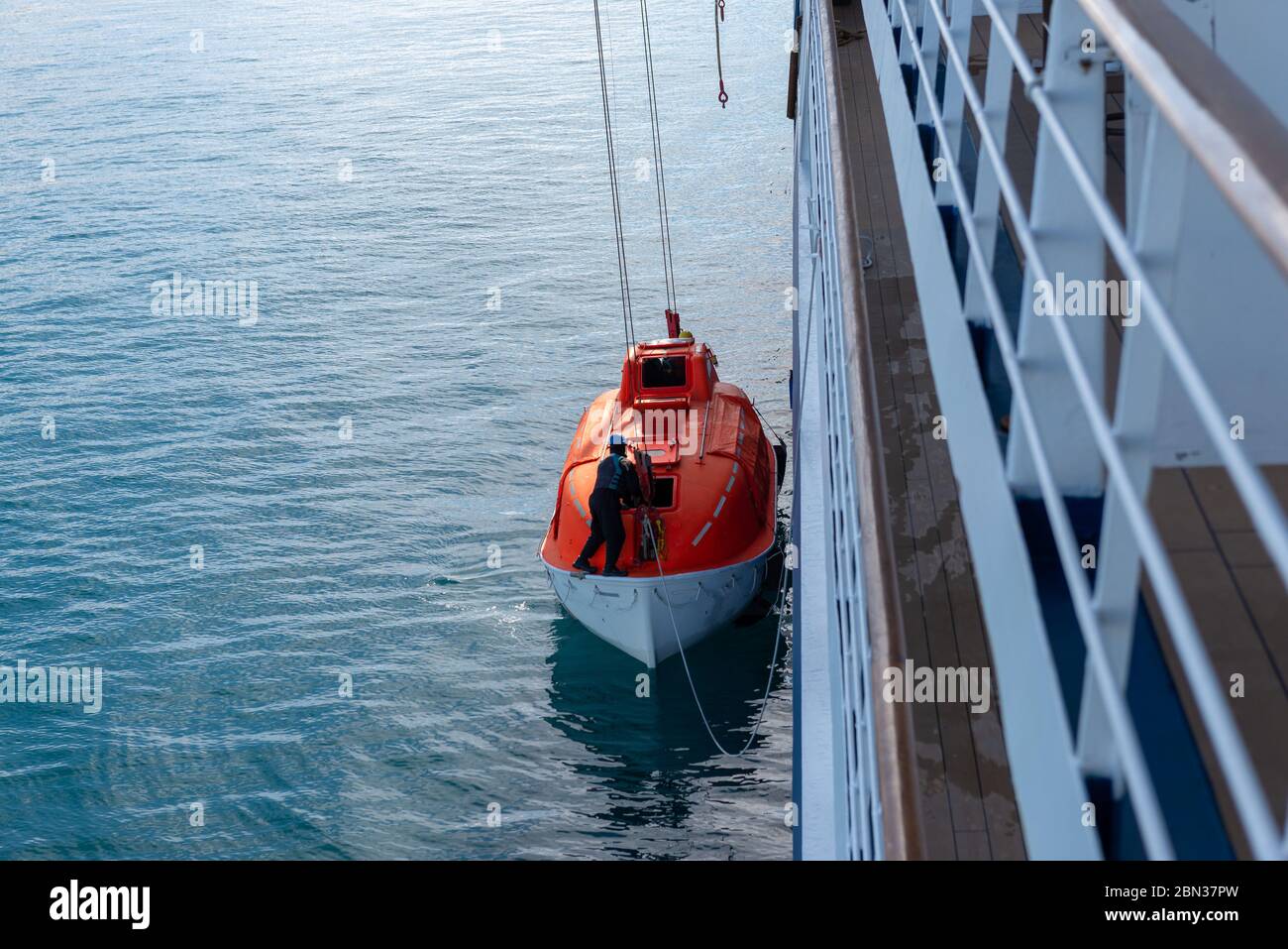 Lowering orange lifeboat to water in Arctic waters, Svalbard. Abandon ...