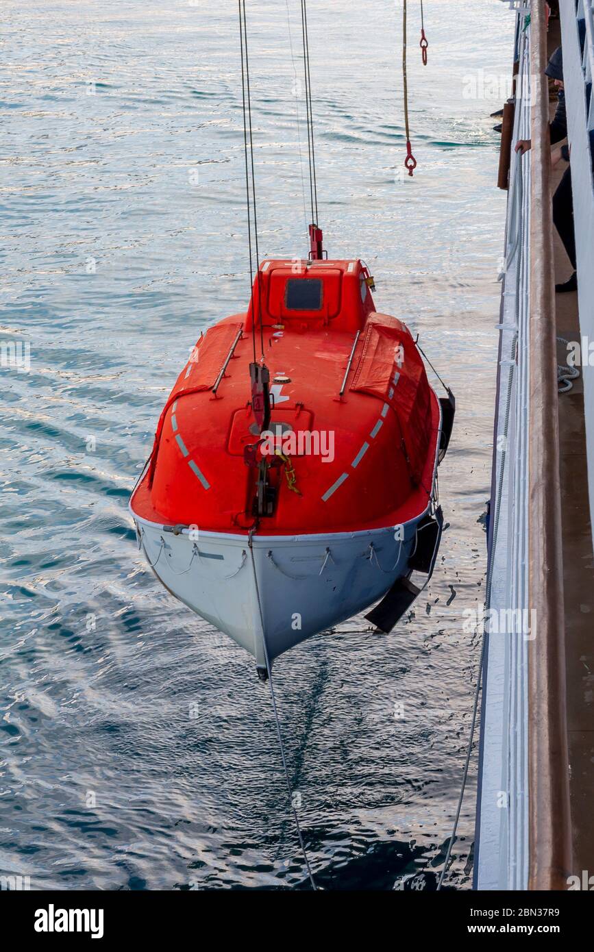 Lowering orange lifeboat to water in Arctic waters, Svalbard. Abandon ...