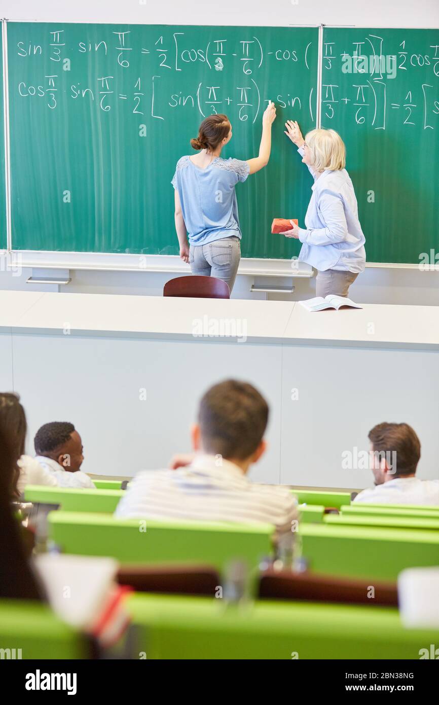 Teacher and student solving math formulas on the blackboard in a ...