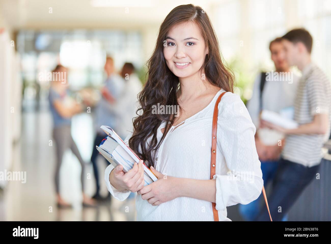 Smiling Asian female student with books in a university aisle Stock ...