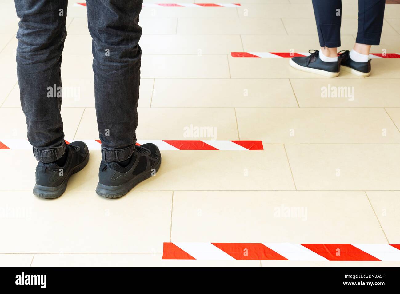 People stand in line keeping social distance, standing behind a warning ...