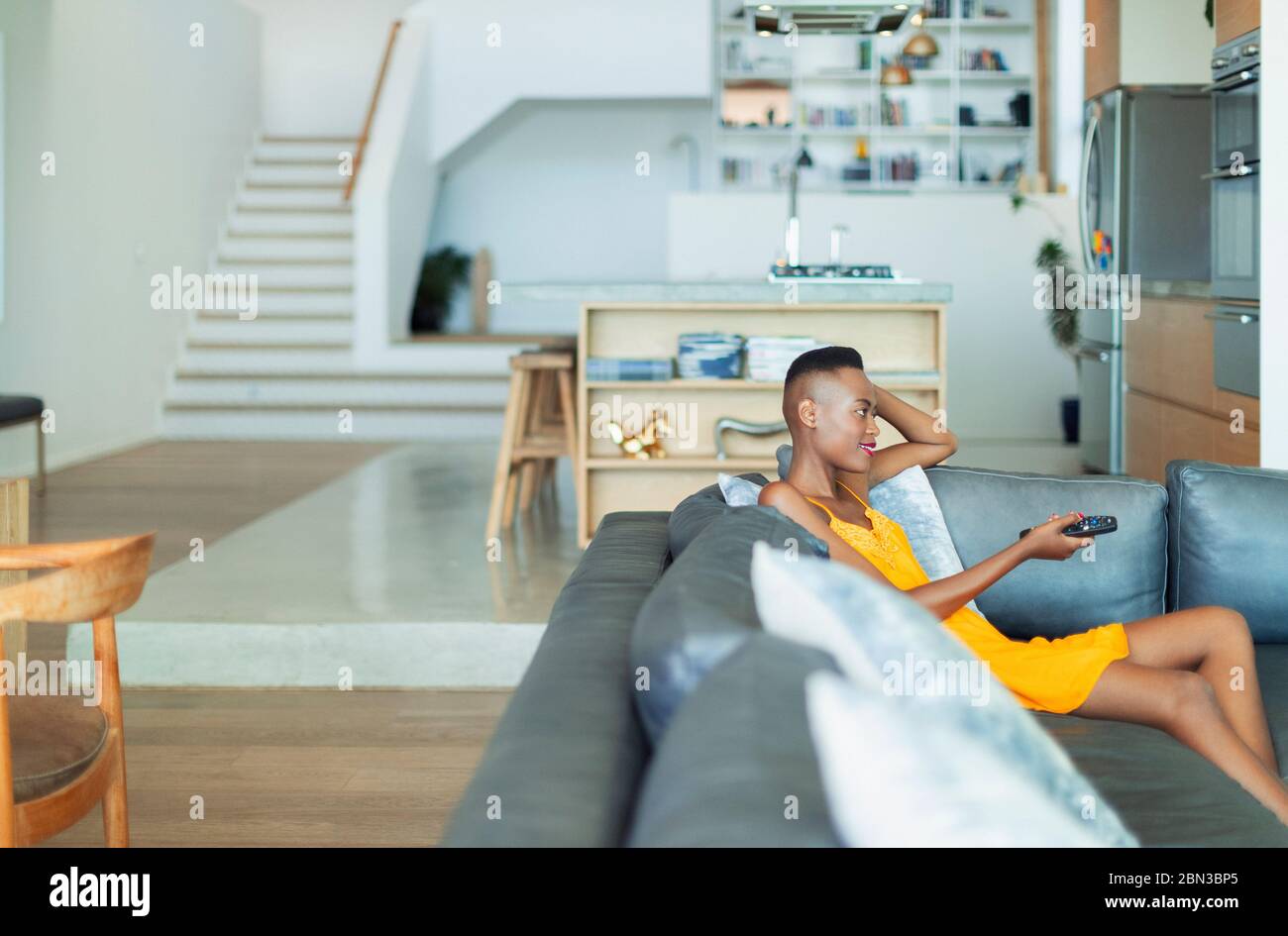 Young woman with remote control watching TV on living room sofa Stock ...
