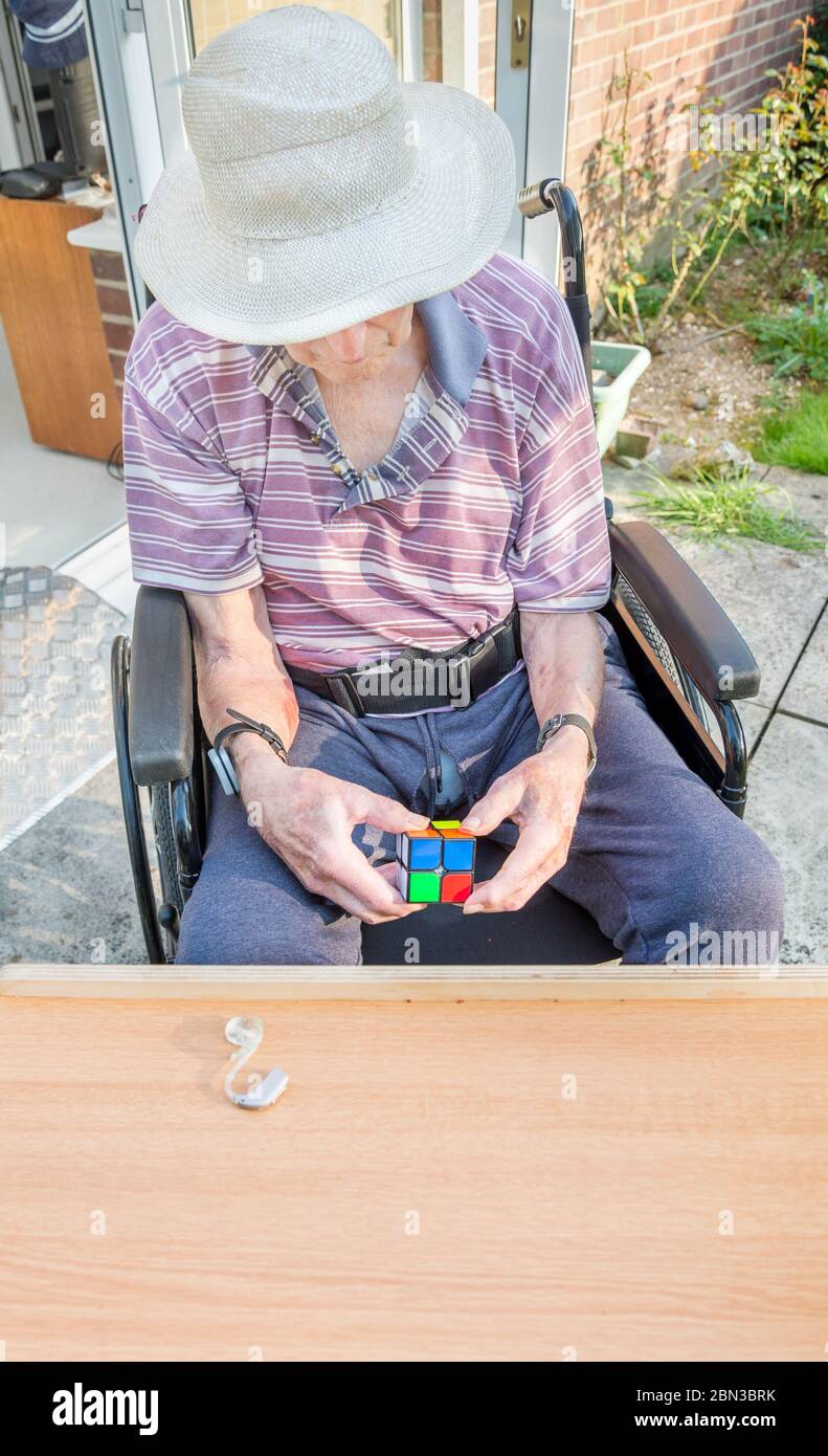 Elderly man seated in a wheelchair uses Rubix cube type puzzle as ...