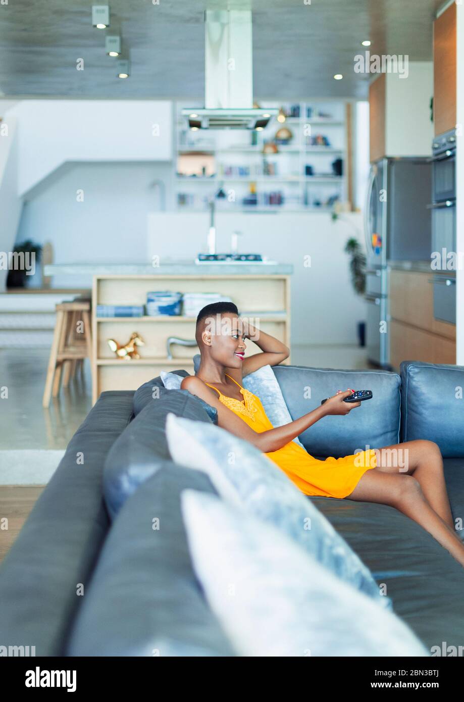 Young woman with remote control watching TV on living room sofa Stock ...