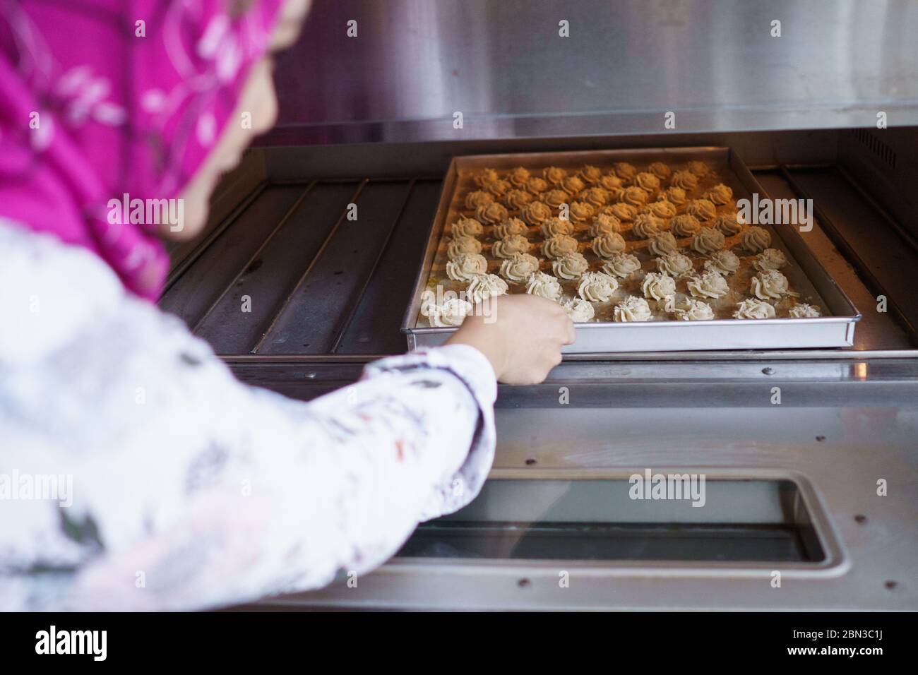 muslim woman put tray of cake into the oven. bakery shop owner working ...
