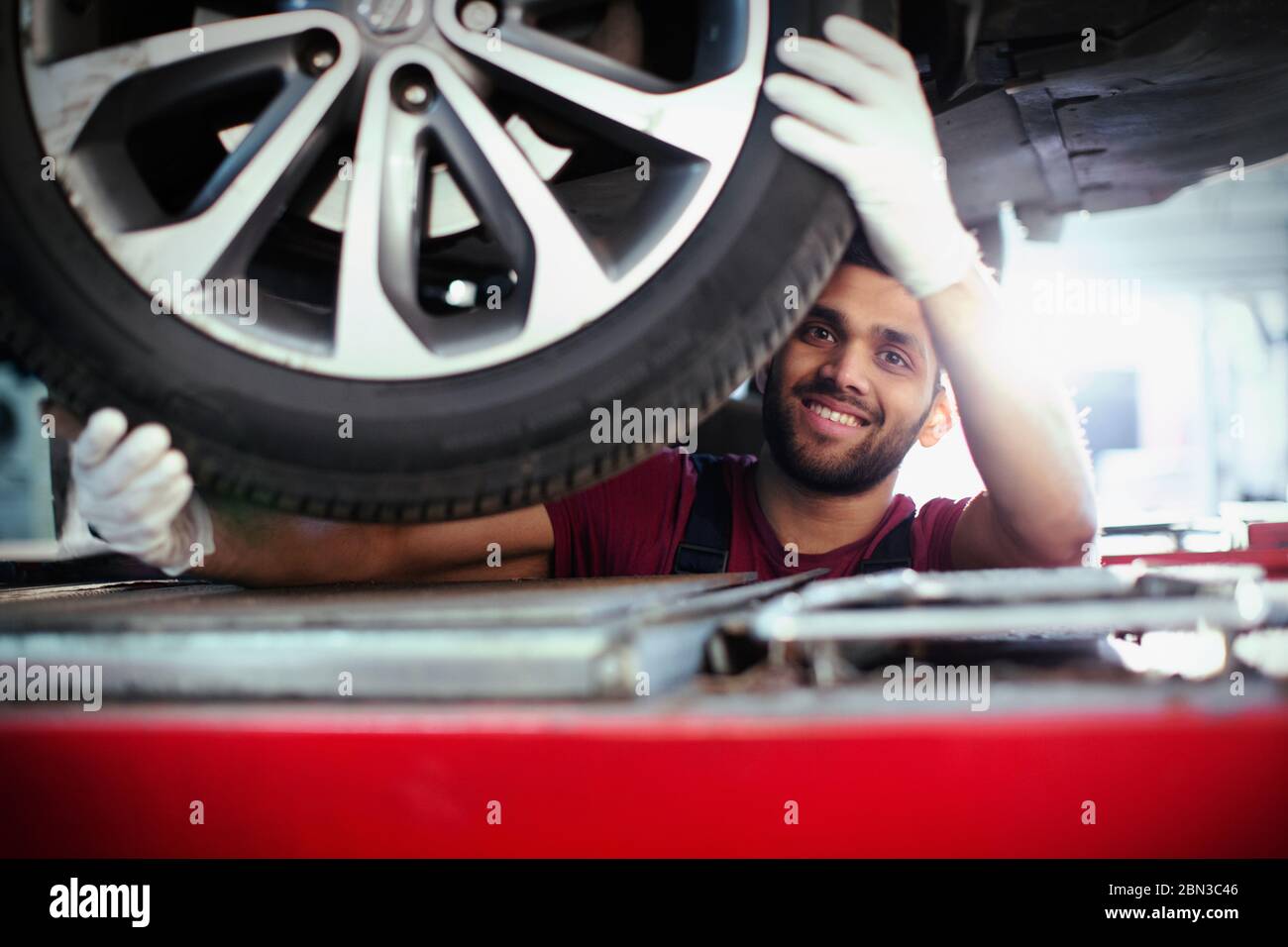 Portrait confident, smiling male mechanic working under car in auto ...