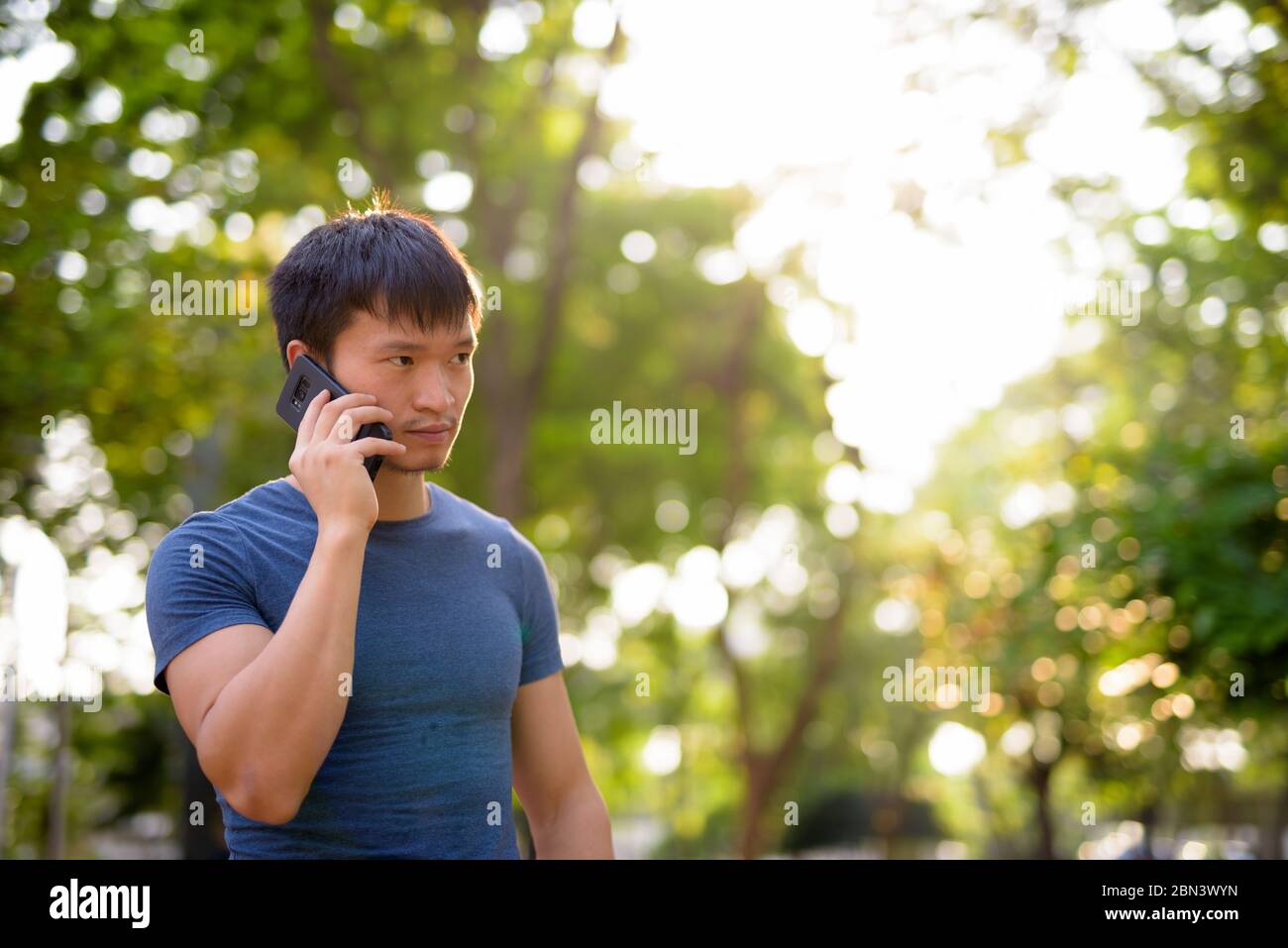 Portrait of young Asian man talking on the phone at the park outdoors ...