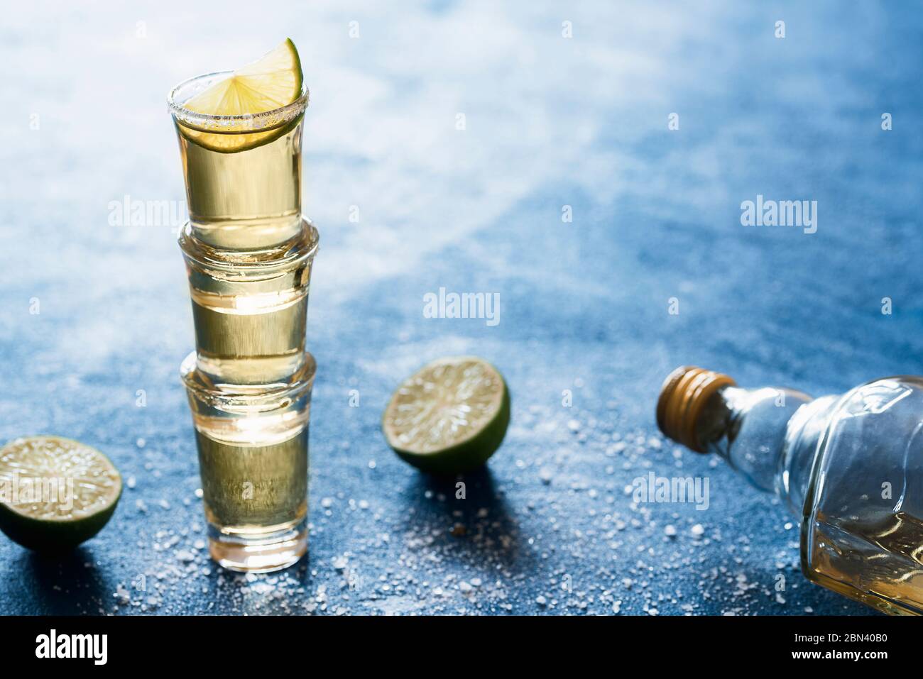 Golden tequila in shot glass with salt and lime, on a blue table ...