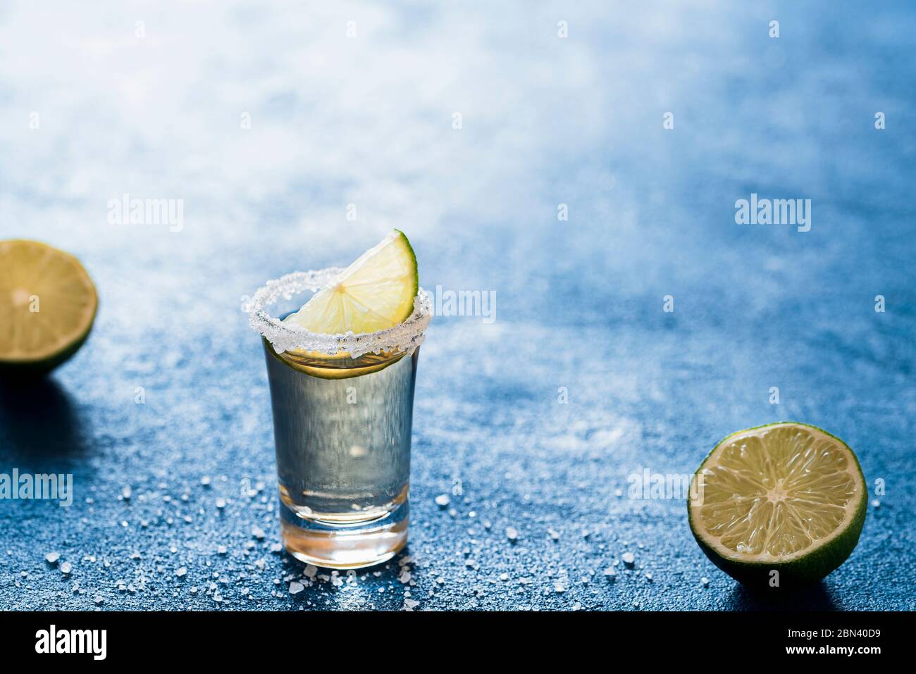 Tequila shot with lime slice and salt on a blue table with backlight ...